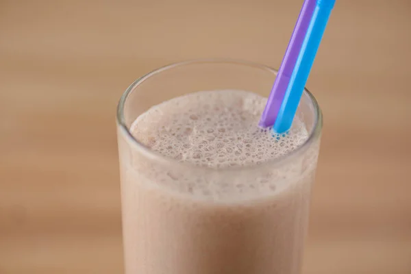 Vanilla chocolate milkshake in a tall galss with two plastic straws on ...