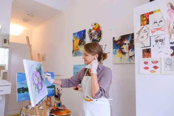 Beautiful young painter paints picture uses brushes and oil, and ...