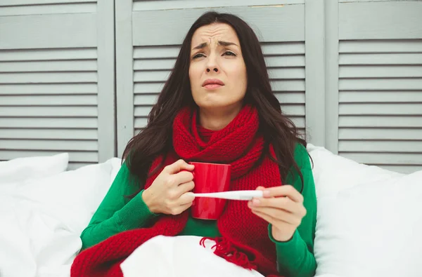 Very high body temperature. A young sick woman in a red scarf measures ...