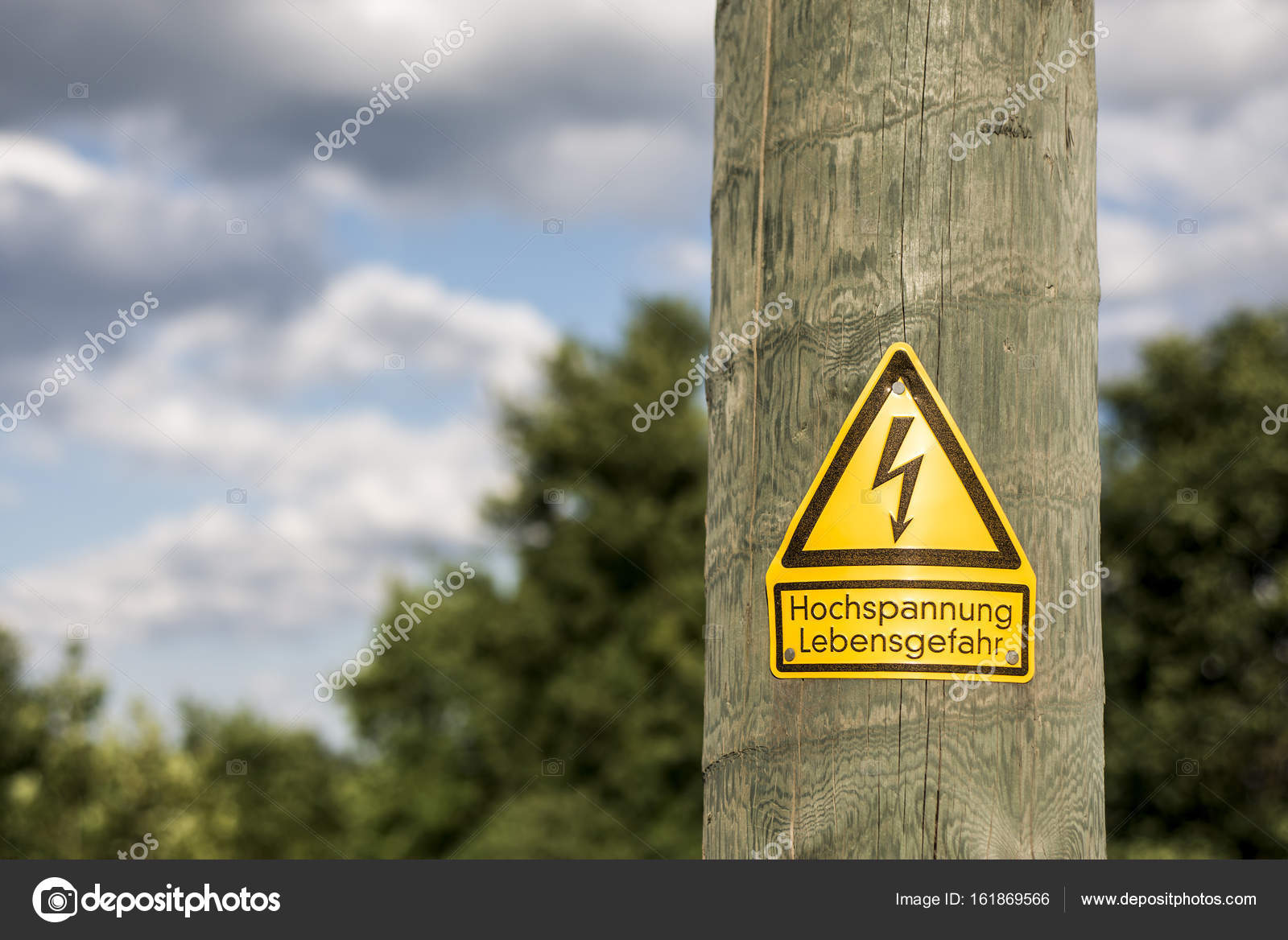 German high voltage sign mounted on wooden pole with green trees in ...