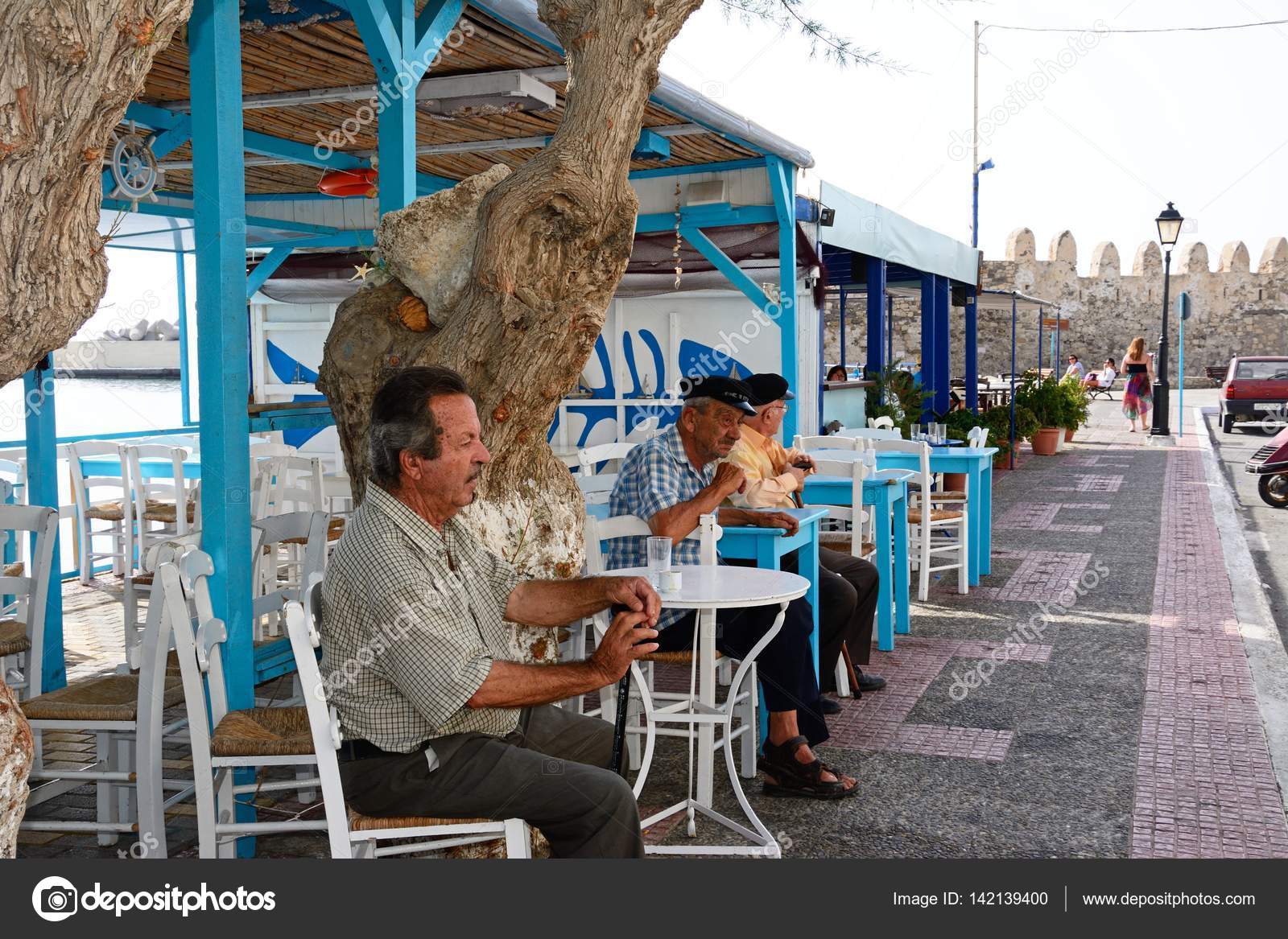 Three elderly Cretan men sitting at a pavement cafe by the harbour ...