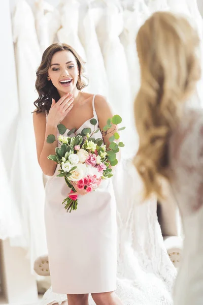 Pretty bridesmaid looking at bride in wedding salon - Stock Image ...