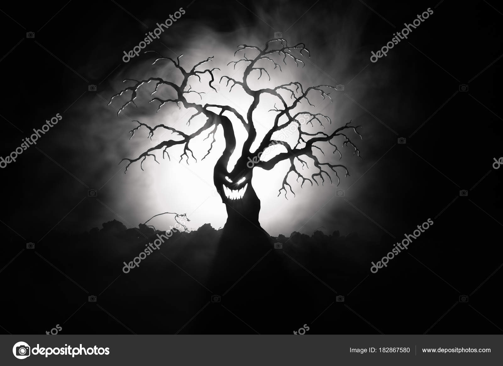 Silhouette of scary Halloween tree with horror face on dark foggy toned ...