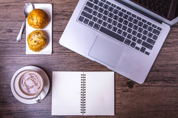 Computer, notebook, tea and bread on wood table for business concept ...