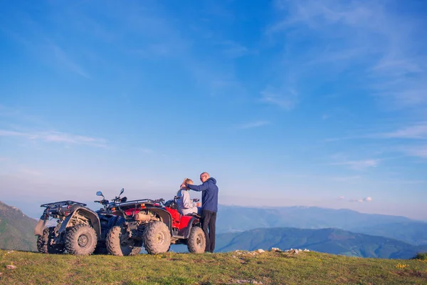Rear view of young pair near atv. Man is showing something in distance ...